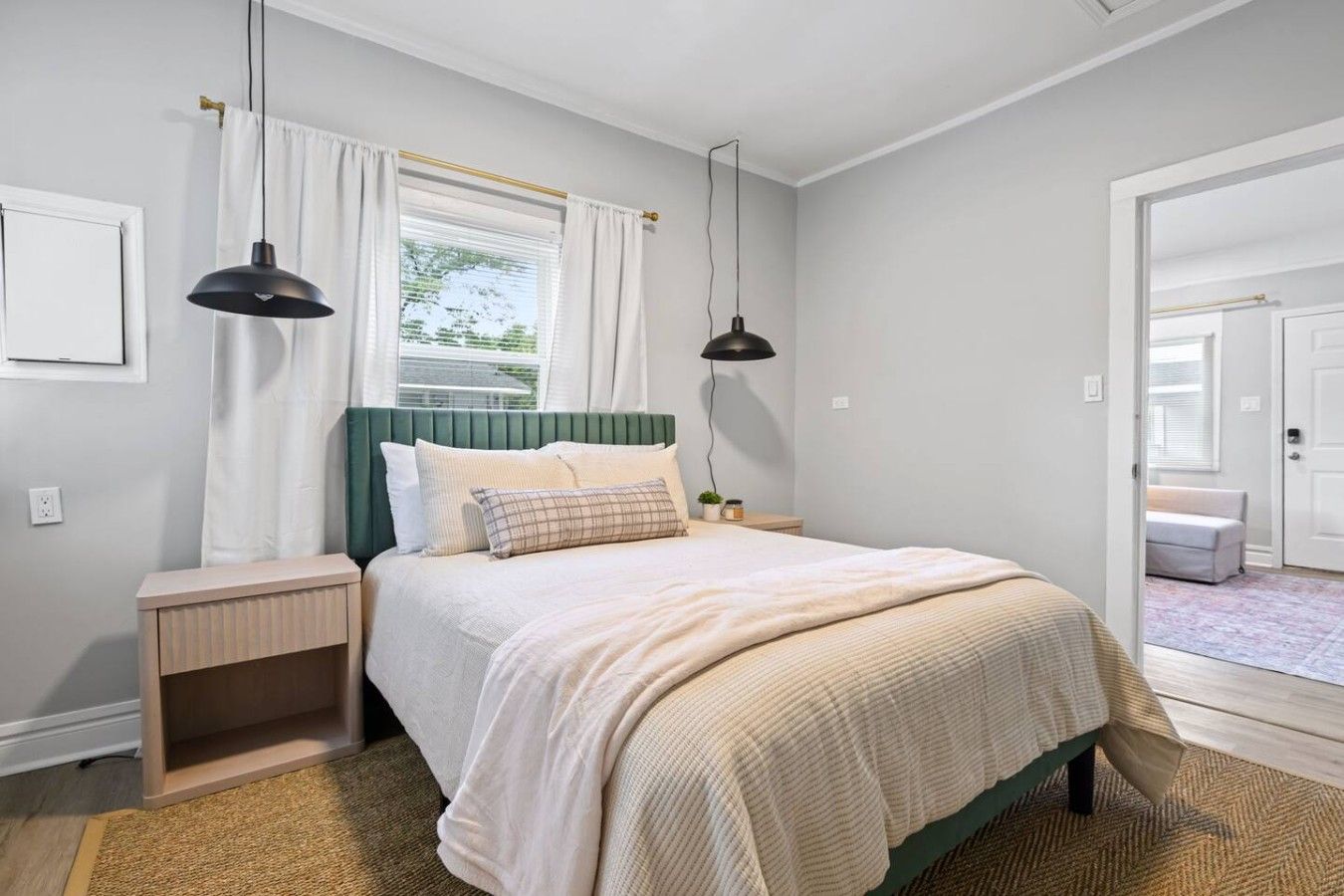 Quarto com cama, mesas de cabeceira, janela com cortinas e porta de acesso a outro cômodo.