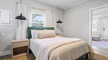 Quarto com cama, mesas de cabeceira, janela com cortinas e porta de acesso a outro cômodo.