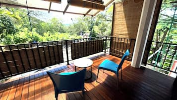 Um deck externo com piso de madeira, duas cadeiras azuis e uma pequena mesa redonda.