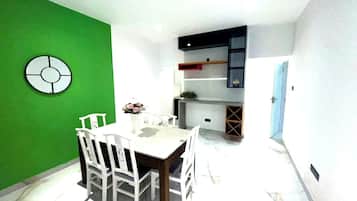 Uma área de refeições com uma parede verde decorativa, uma mesa branca e cadeiras.