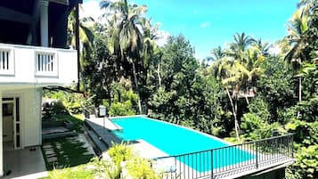 Piscina cercada por vegetação exuberante e um edifício de dois andares com varanda.