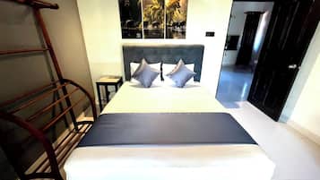 Quarto de hotel com cama, escada de madeira, prateleira na parede e porta que dá para outro cômodo.