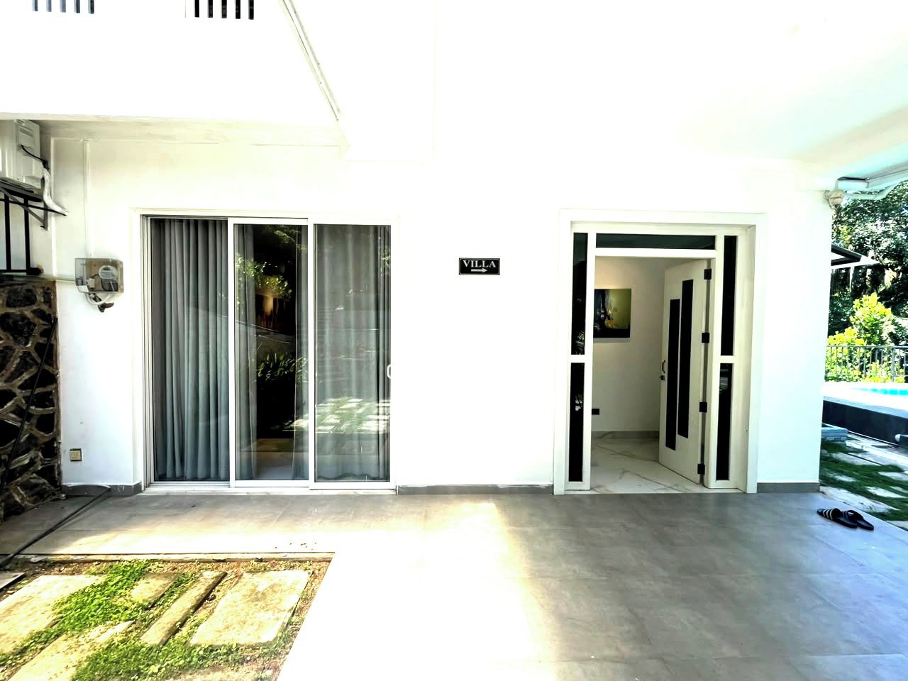 Uma casa moderna com parede de pedra, porta de vidro deslizante e pátio de concreto.
