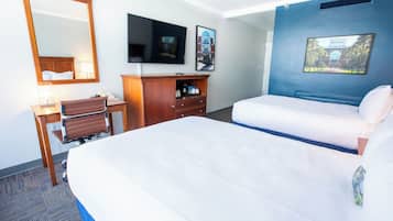 Quarto de hotel com uma cama grande, uma escrivaninha com cadeira, televisão e um quadro na parede.
