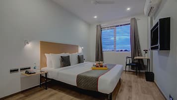 Quarto de hotel com cama, mesa de cabeceira, janela e escrivaninha com cadeira.