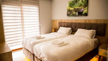Uma cama de casal com cabeceira de madeira, duas mesas de cabeceira e um quadro de um jardim na parede.