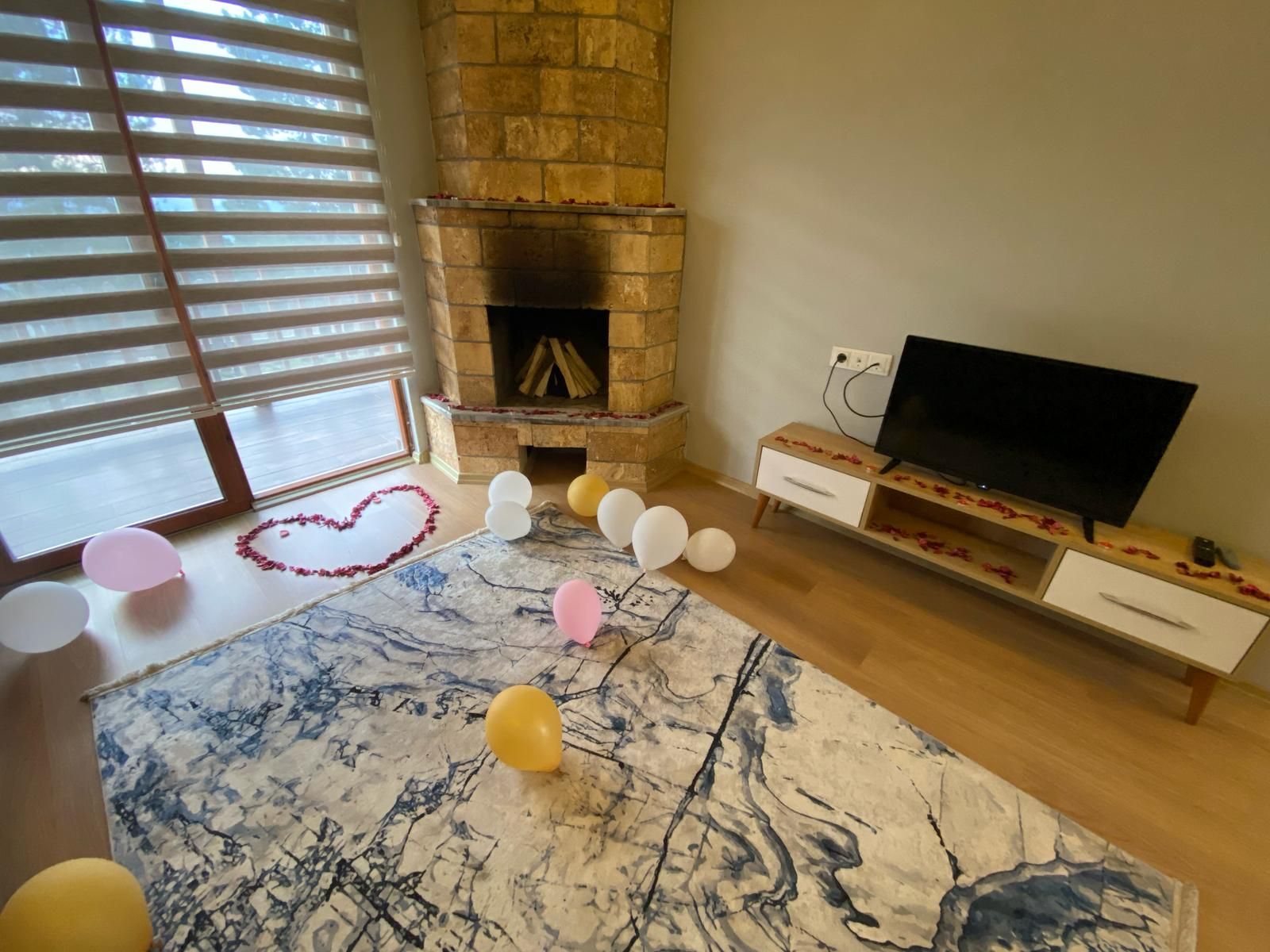 Sala de estar com lareira de pedra, televisão de tela plana e tapete com padrão marmorizado.