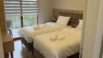 Quarto com duas camas, cabeceira de madeira, escrivaninha e uma cadeira.