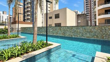 Piscina com água azul cristalina, cercada por um muro de pedra e ladeada por um deck revestido com azulejos.