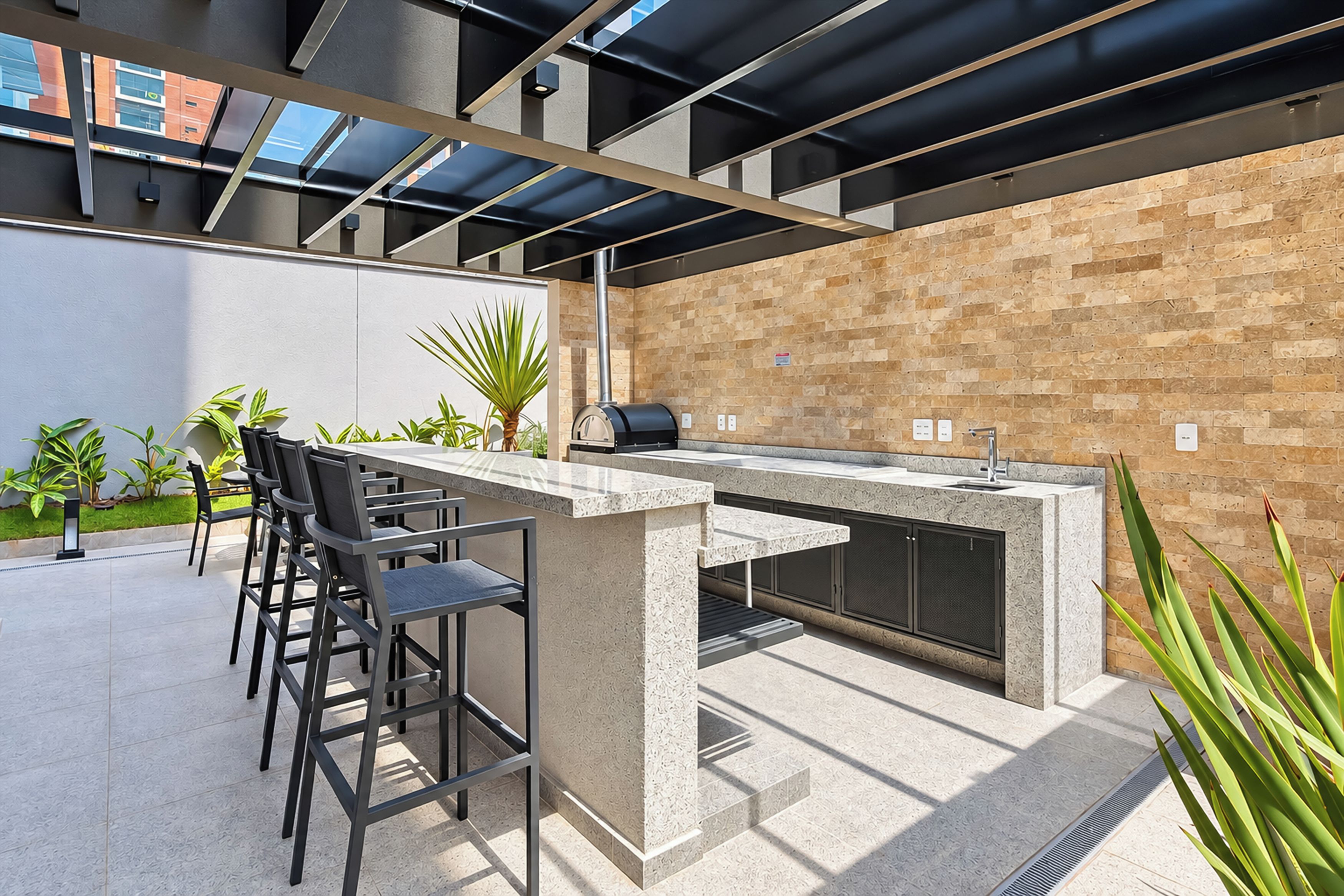Uma área de cozinha externa com churrasqueira embutida, banquetas de bar e painel de fundo de pedra.