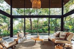 Um quarto amplo, com grandes janelas, teto de madeira e uma mesa central com cadeiras.