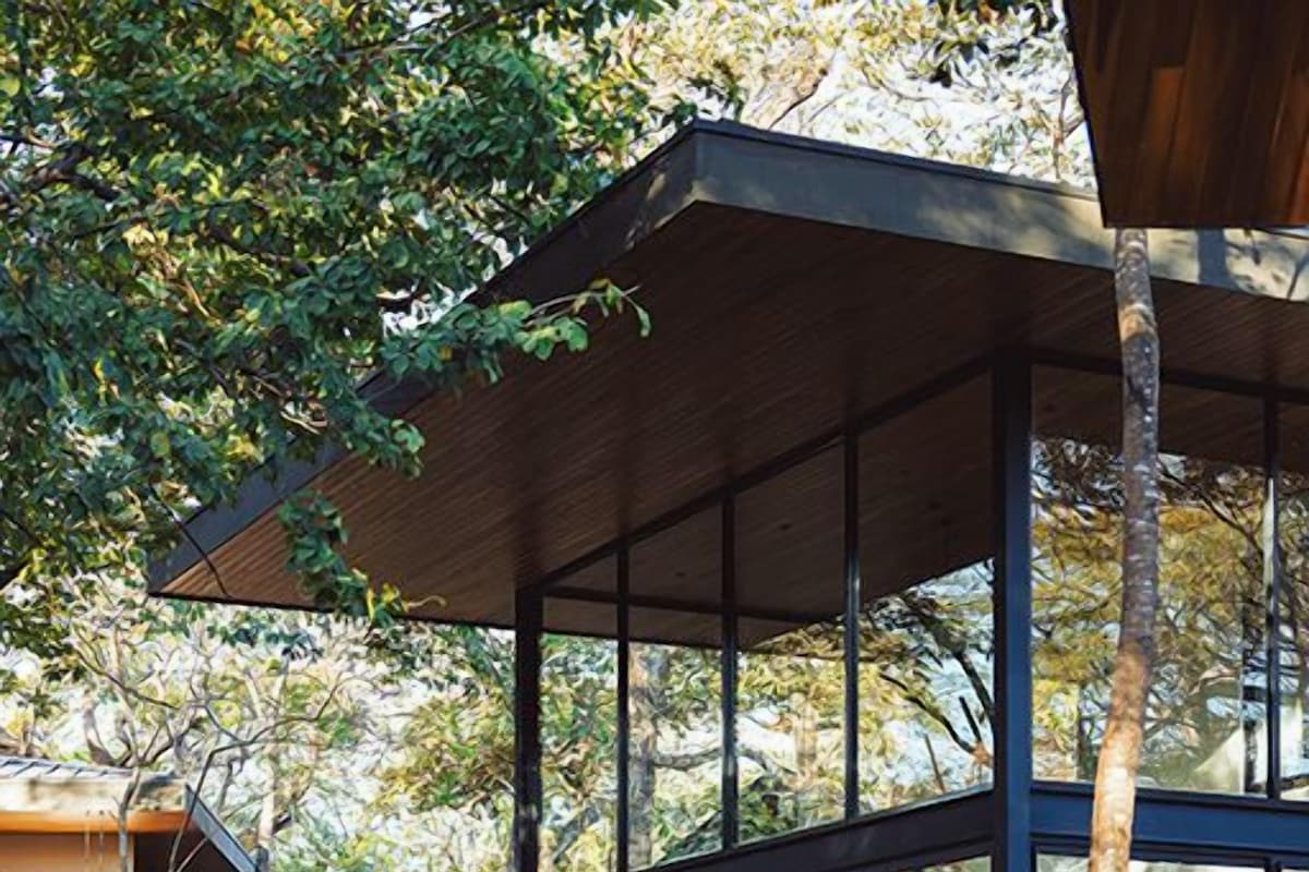 Estrutura moderna ao ar livre com paredes de vidro, rodeada por vegetação exuberante e uma piscina refletora.