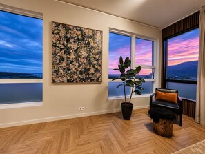 Quarto com uma grande janela, uma planta em vaso, uma cadeira e um quadro na parede.