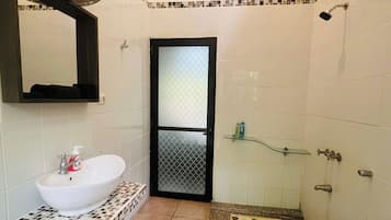 Casa de banho com lavatório branco, espelho, zona de duche e chão em azulejos.