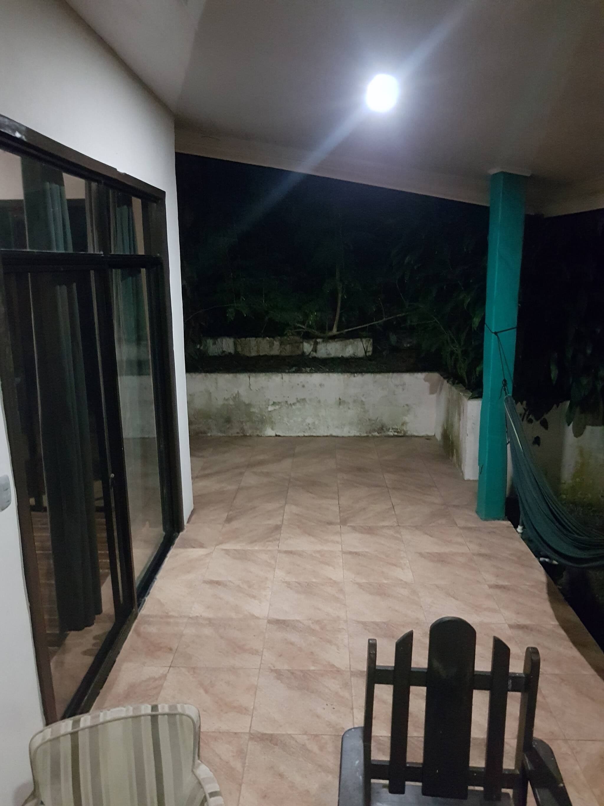 Uma área de estar ao ar livre com piso de azulejos, uma rede e uma cadeira.