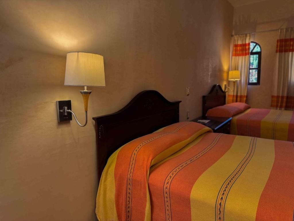 Quarto de hotel com cama, luminária de cabeceira, janela com cortinas e luminária na parede.