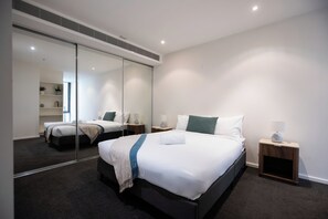 Quarto de hotel moderno com uma cama grande, mesas de cabeceira, um espelho e vista para o quarto vizinho.