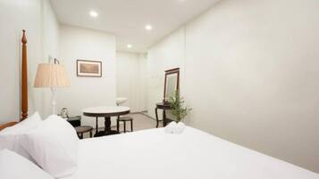 Quarto de hotel com cama, mesa redonda, cadeira, luminária, quadro emoldurado e espelho.