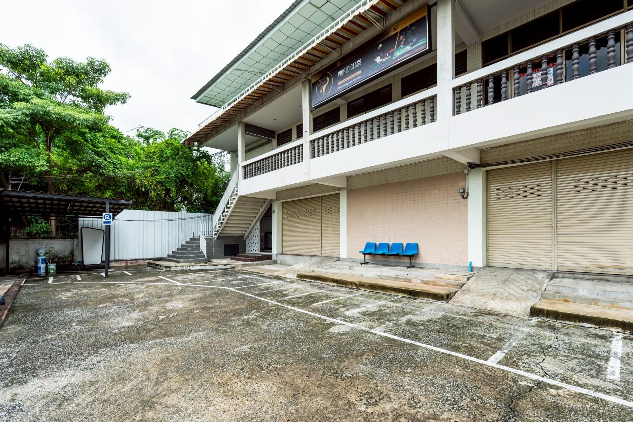 Um edifício com área externa coberta, escadaria e fileira de cadeiras azuis.