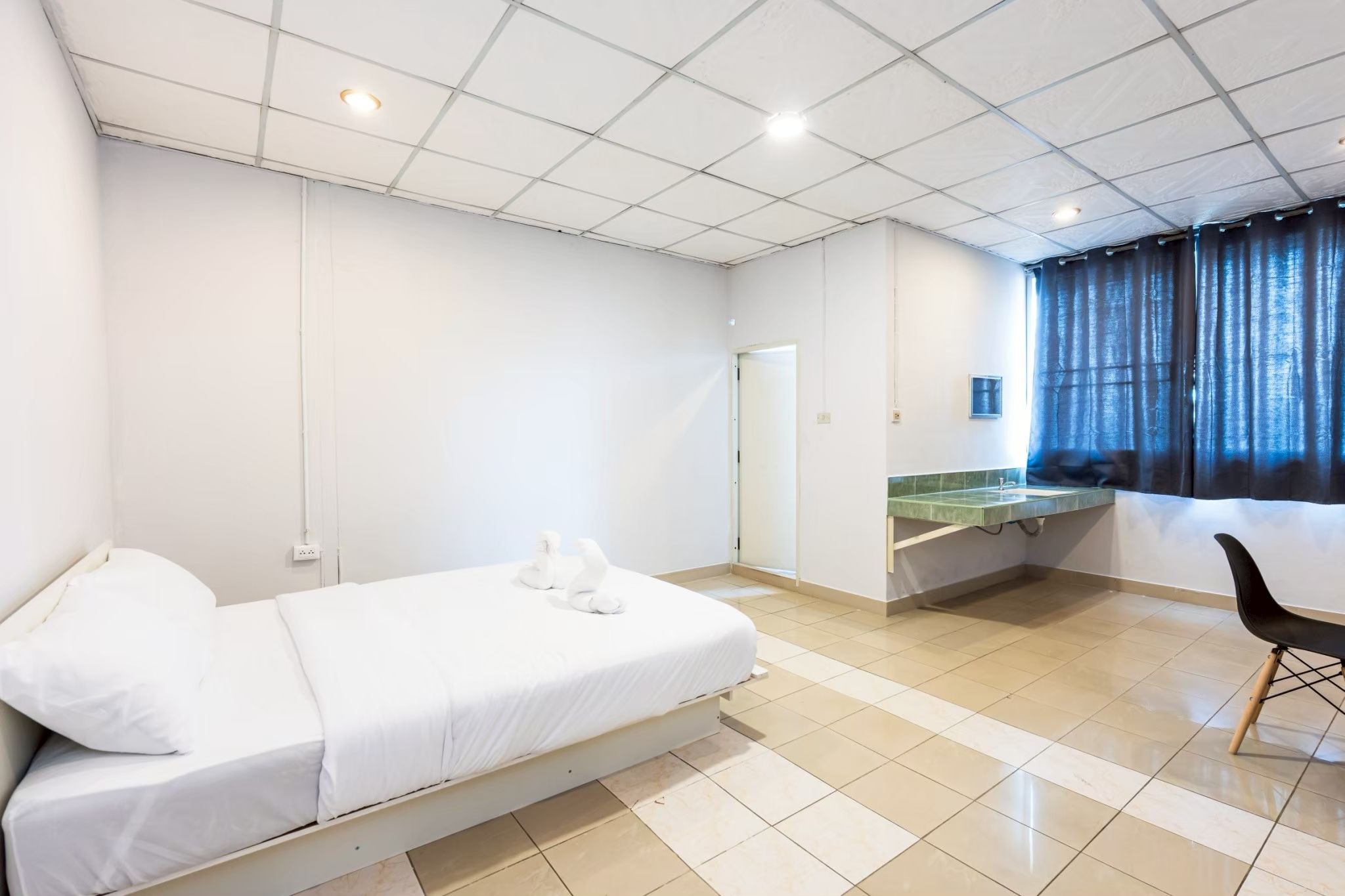 Quarto de hotel com cama, escrivaninha, cadeira e banheiro com pia e espelho.