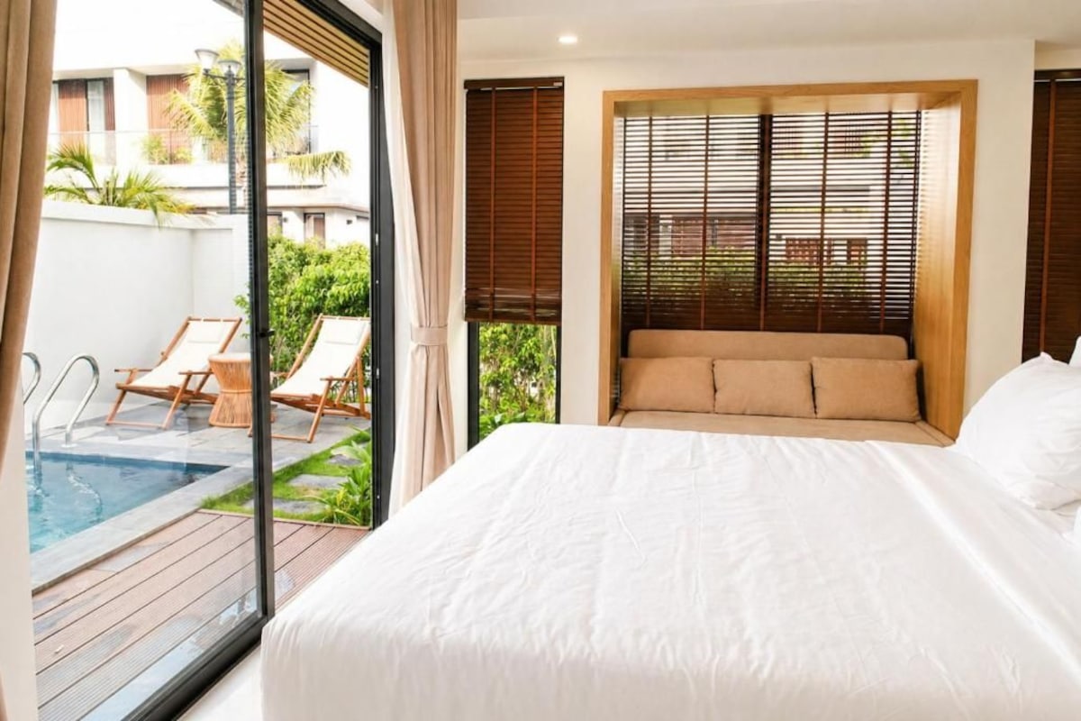 Quarto com cama grande, vista para uma piscina e varanda com cadeiras.