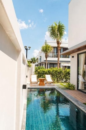 Piscina com espreguiçadeiras e uma palmeira, cercada por edifícios modernos.