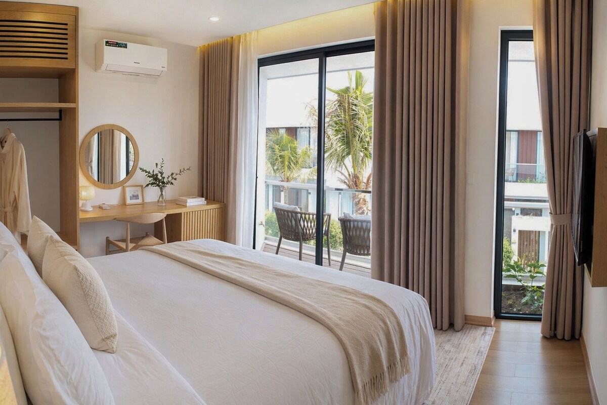 Quarto de hotel com uma cama grande, uma escrivaninha com espelho e vista para uma varanda com mobiliário de exterior.