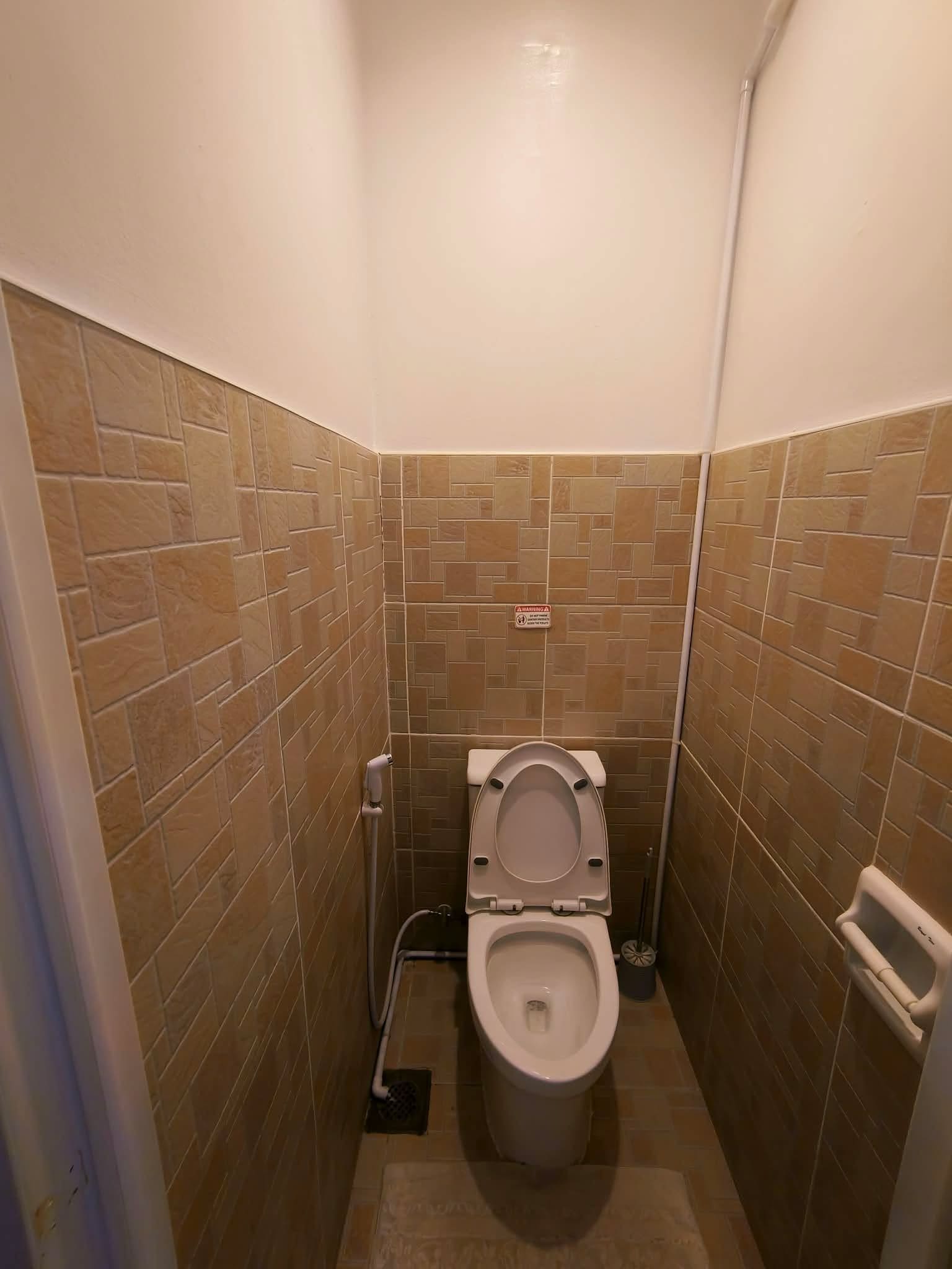 Casa de banho pequena com azulejos, sanitário, secador de mãos e vassoura.