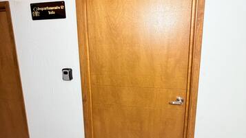Uma porta de madeira com maçaneta de metal, uma placa acima e um interruptor de luz na parede.