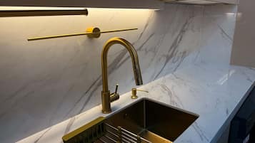 Cozinha com pia moderna de aço inoxidável, bancada de mármore e torneira dourada.