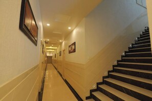 Um corredor de hotel com piso de mármore, escadaria e quadros emoldurados nas paredes.