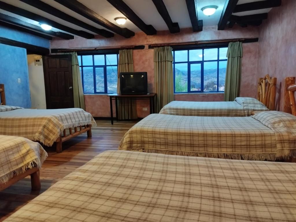 Quarto com quatro camas, televisão e vista para o exterior através de amplas janelas.