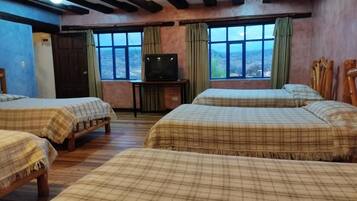 Quarto com quatro camas, televisão e vista para o exterior através de amplas janelas.