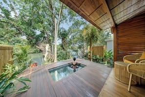 Um deck de madeira com uma banheira de hidromassagem, cercado por vegetação exuberante e vista para um rio.
