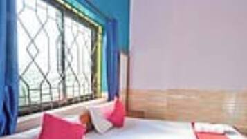 Quarto com cama, janela com grade decorativa e parede azul.