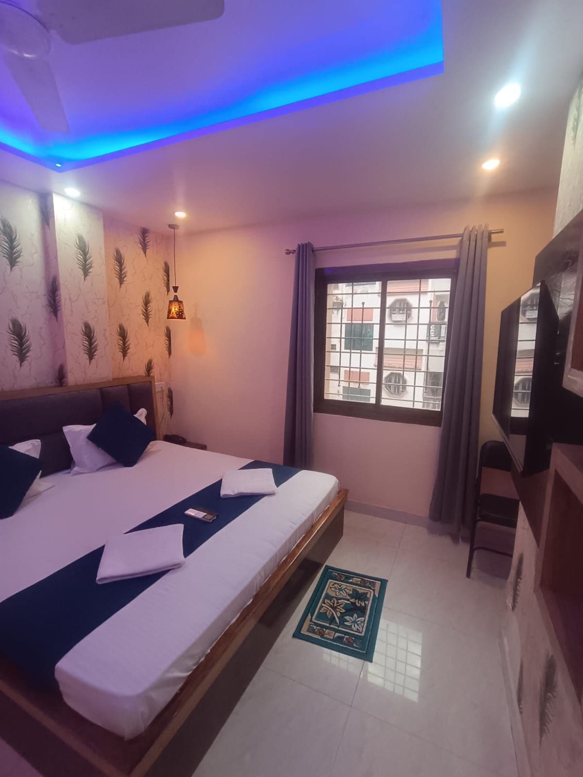 Quarto de hotel com cama, televisão, janela com cortinas e um detalhe decorativo na parede.