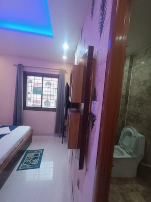 Quarto com cama, janela com cortinas, porta com espelho e um vaso sanitário.