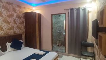 Quarto de hotel com cama, ventoinha no teto, área de chuveiro e televisão na parede.