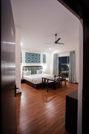 Quarto de hotel com cama, mesa com cadeiras, ventilador de teto e janela com cortinas.