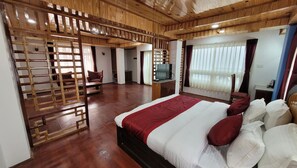 Quarto de hotel com uma cama grande, televisão, teto de madeira e janela com cortinas.