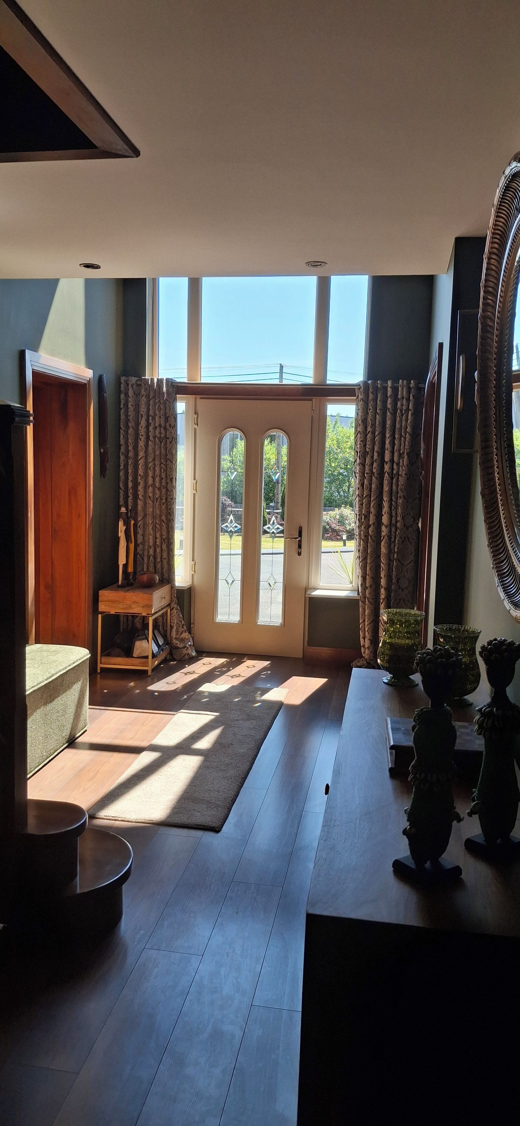Quarto com piso de madeira, porta com painéis de vidro, uma mesa pequena e janela com cortinas.