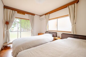 Quarto de hotel com duas camas, uma janela com cortinas, cabeceira de madeira e uma pequena mesa de cabeceira.