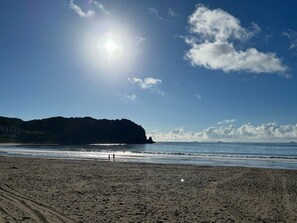 Uma praia com céu claro, um sol grande e um relevo distante.