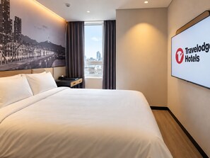 Quarto de hotel com uma cama grande, mesa de cabeceira, janela com cortinas, um mural com paisagem urbana e um letreiro Travelodge Hotels.
