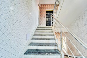 Uma escadaria com degraus de mármore conduzindo a uma porta, com um padrão geométrico nas paredes.