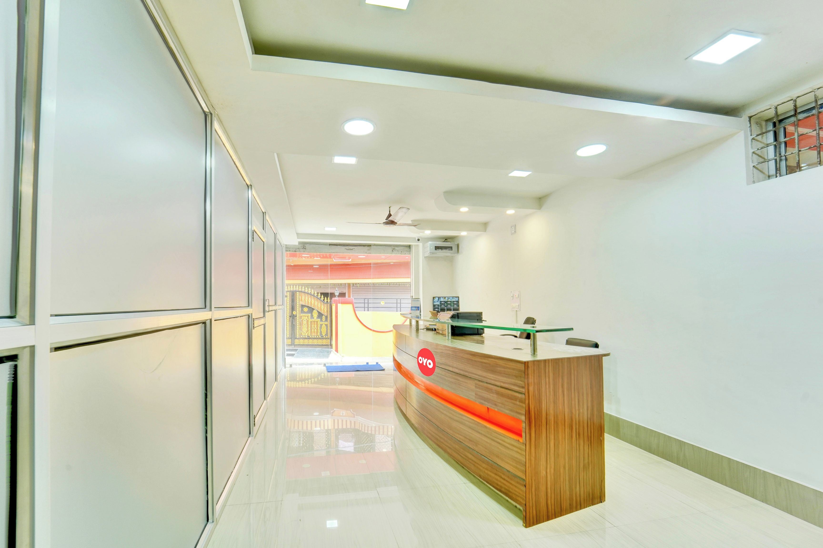 Balcão de recepção com design moderno, um ventilador de teto e vista para um portão vermelho ao fundo.