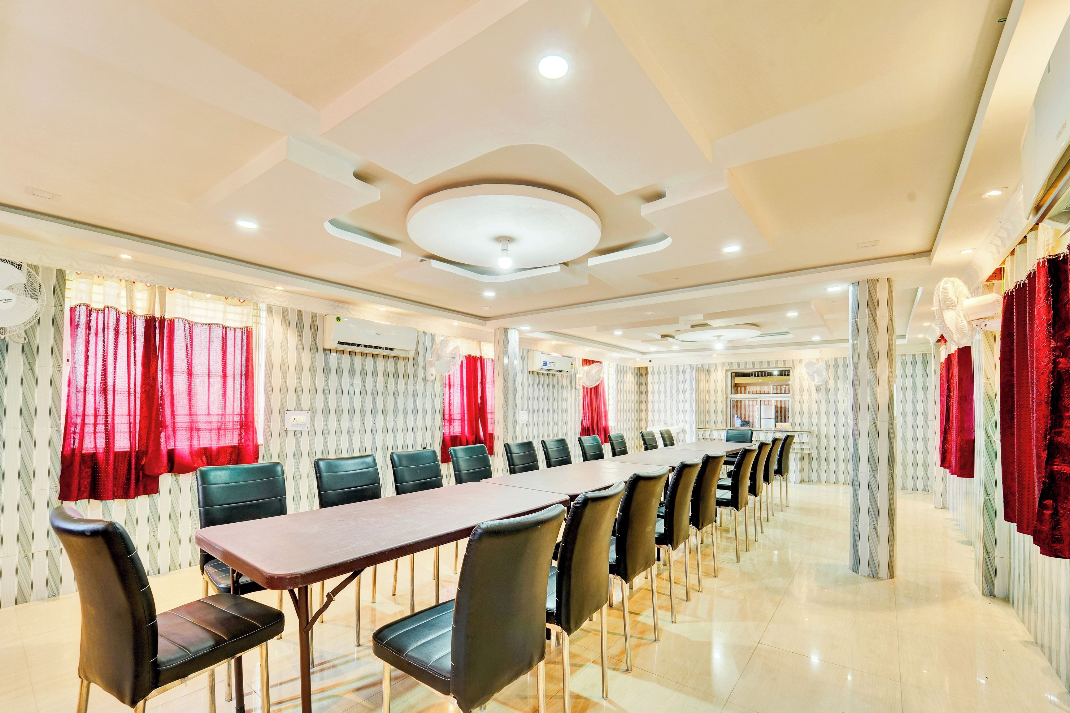 Sala de conferências com uma mesa comprida e cadeiras, aparelhos de ar condicionado e cortinas estampadas.