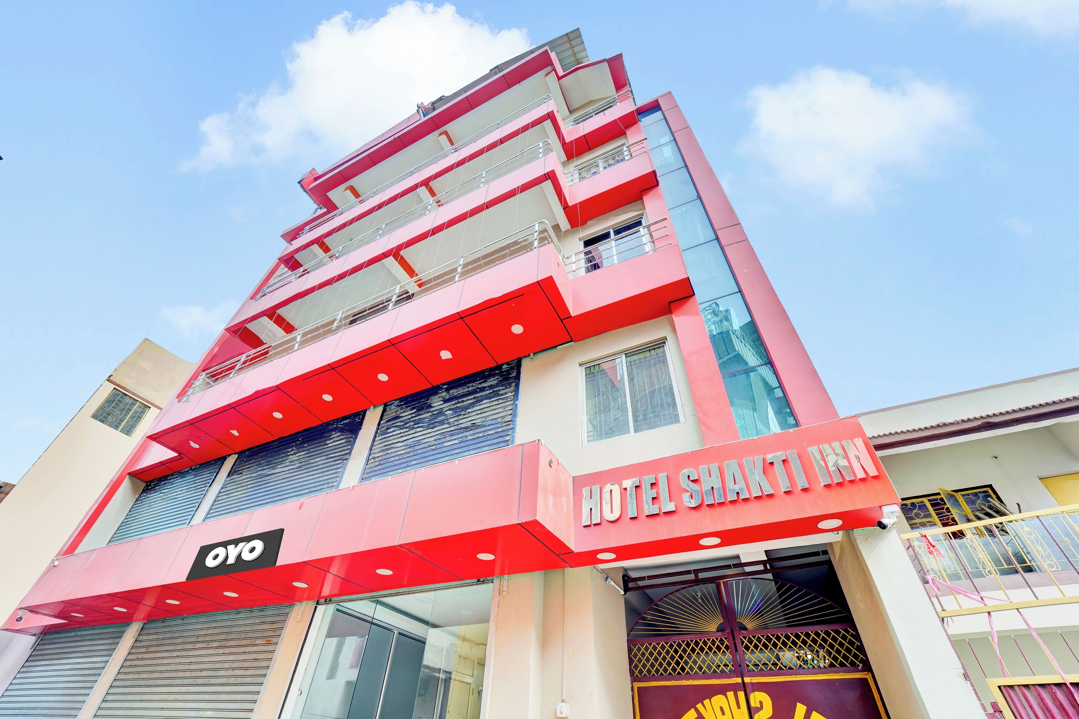 Um hotel com vários andares, varandas e um letreiro chamativo com a inscrição 'HOTEL SHAKTI INN'.