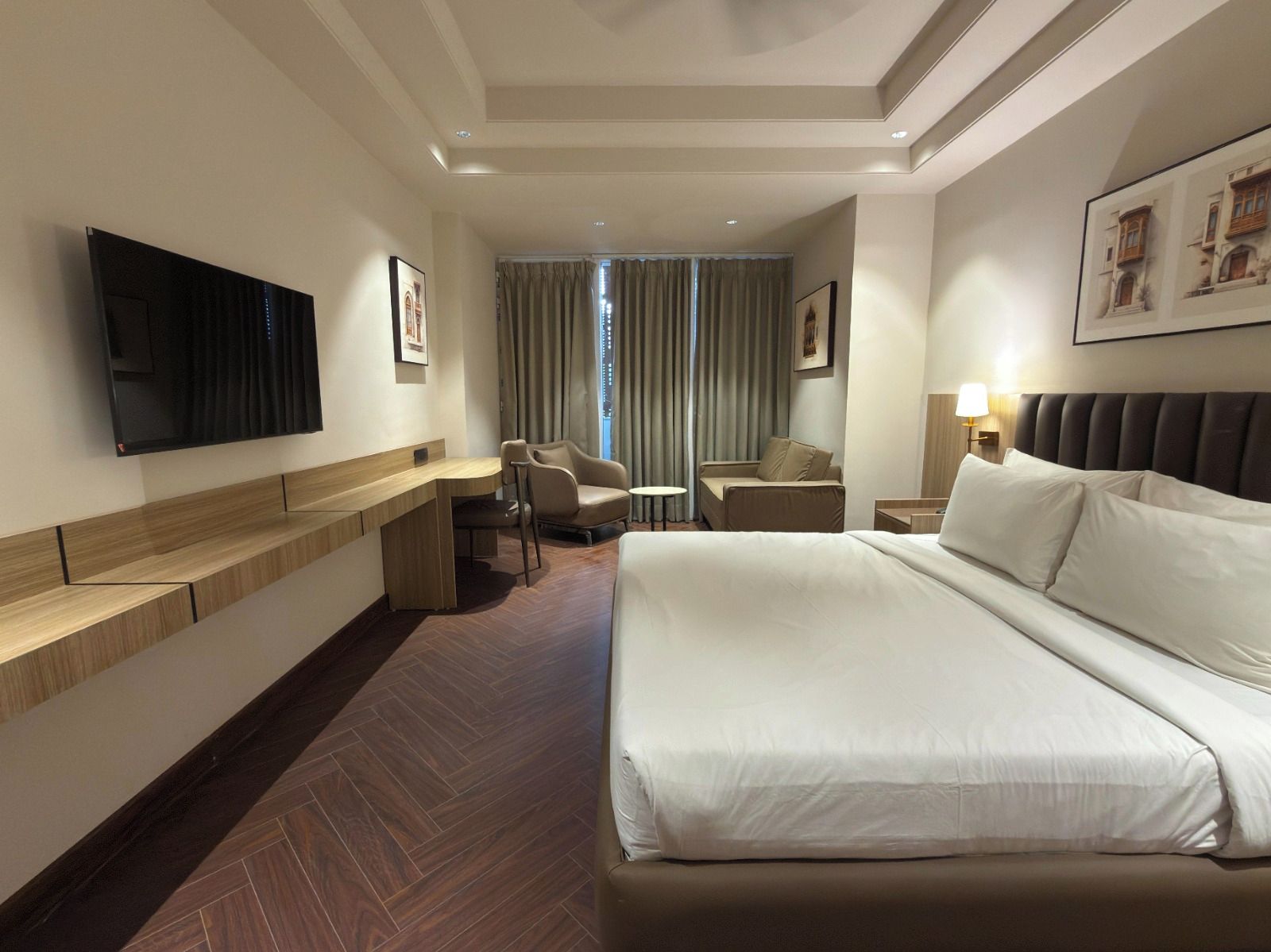 Quarto de hotel com cama, escrivaninha, cadeira, televisão e janela com cortinas.