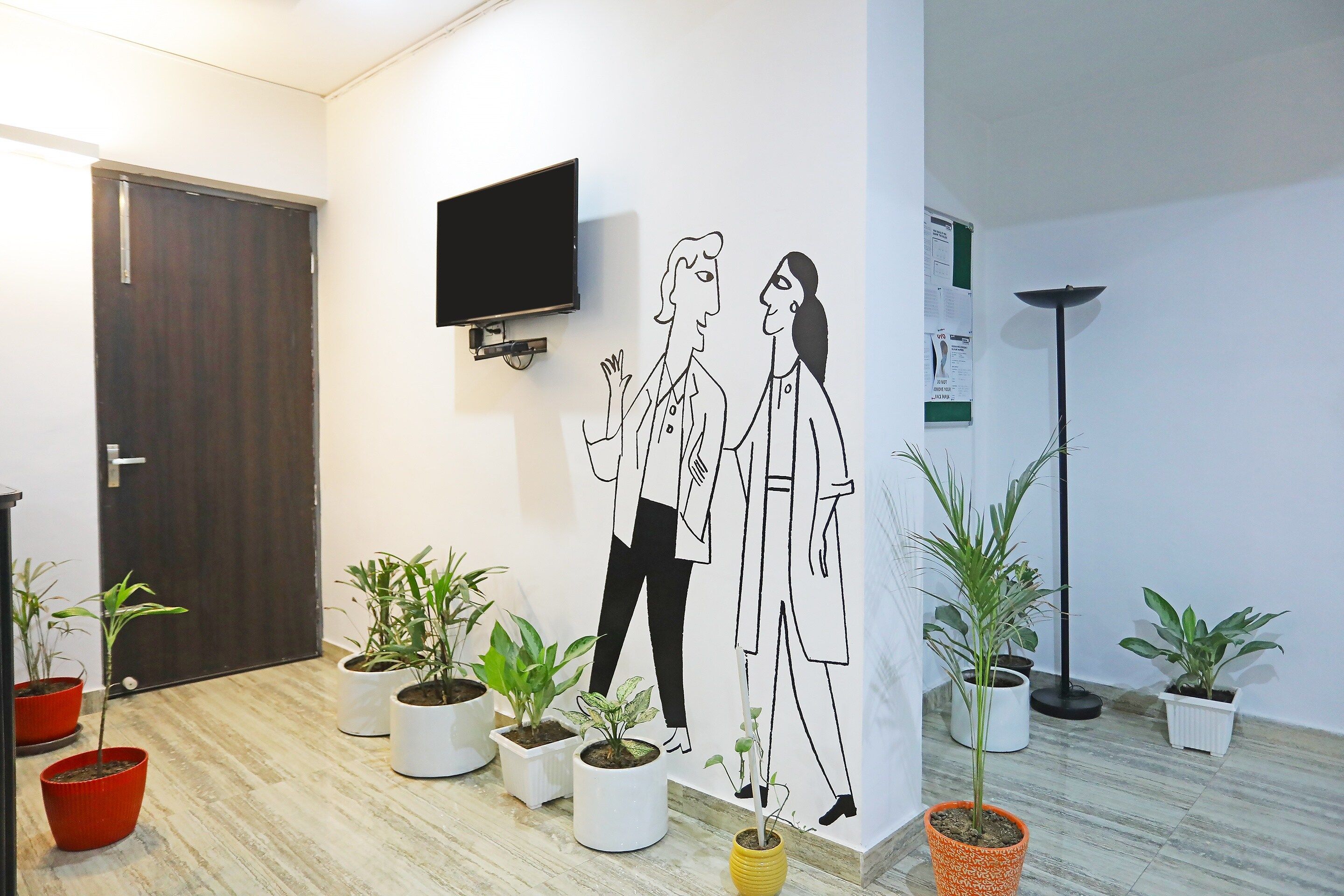 Um corredor com televisão de tela plana na parede, plantas em vasos e uma porta.